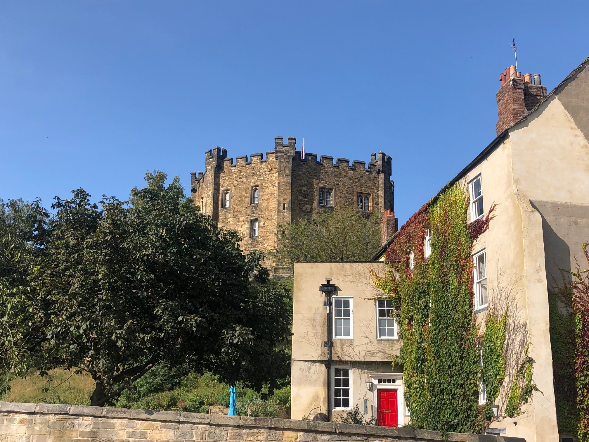 Part of Durham Castle on a sunny day, with a house covered in ivy in the foreground